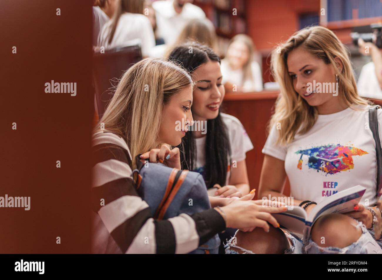 Three young and beautiful students reading the books and laughing at ...