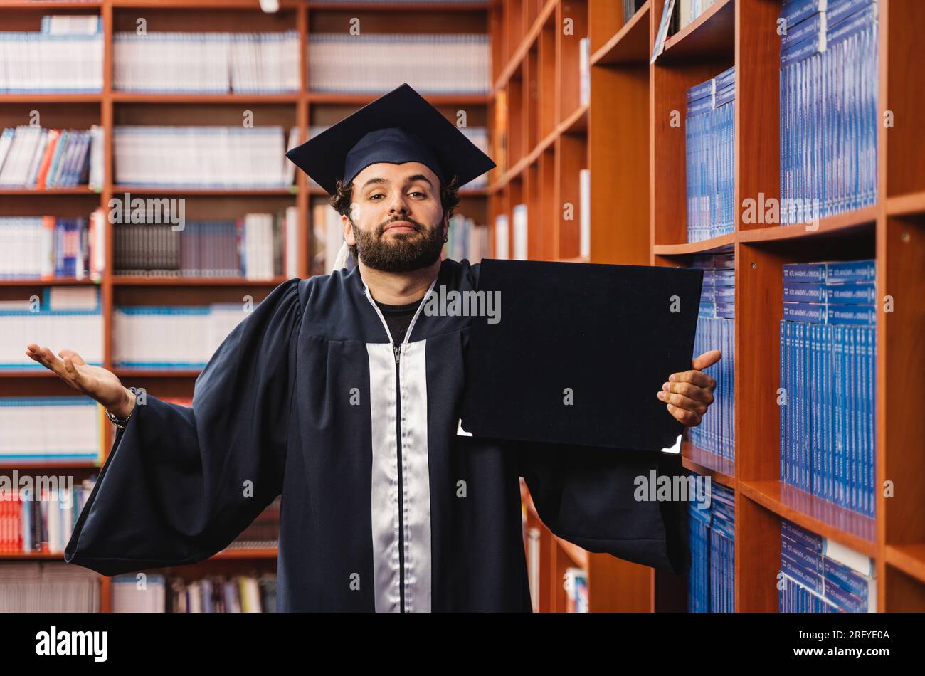 Young and happy graduate wearing a cap and gown and holding his ...