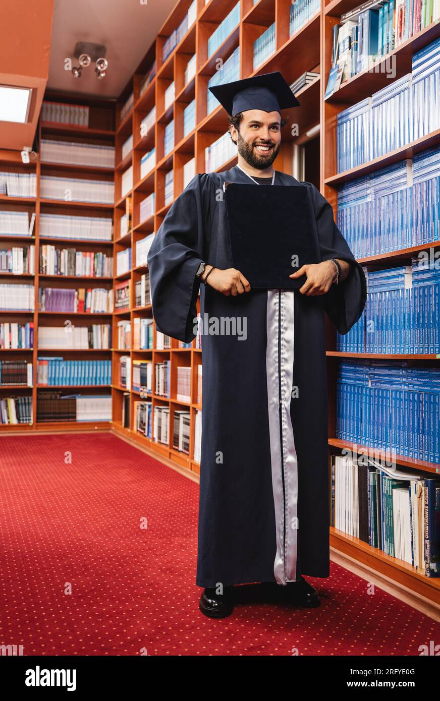 Young and happy graduate wearing a cap and gown and holding his ...