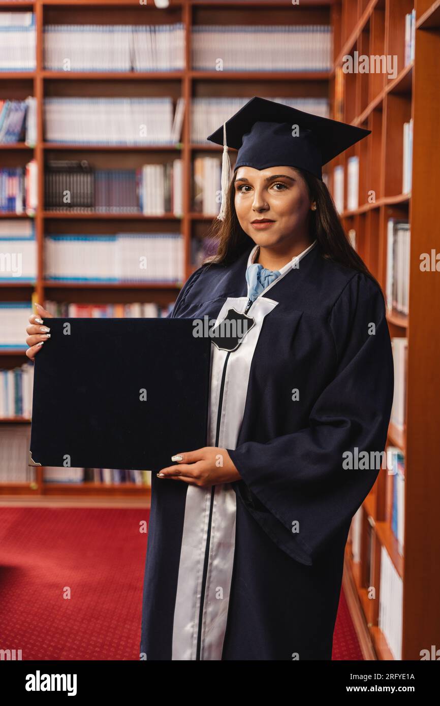 Young graduate holding her bachelor's degree and wearing a cap and gown ...