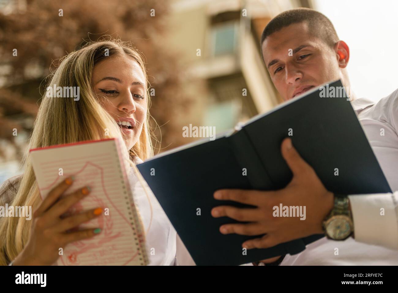Two young students standing outside with notebooks in their hands and ...