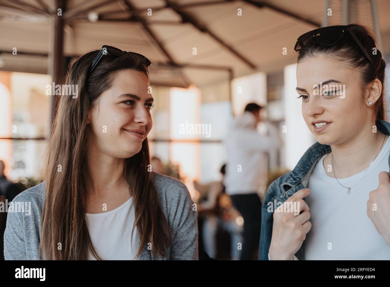 Close up of two beautiful brunette girls talking while sitting at the ...