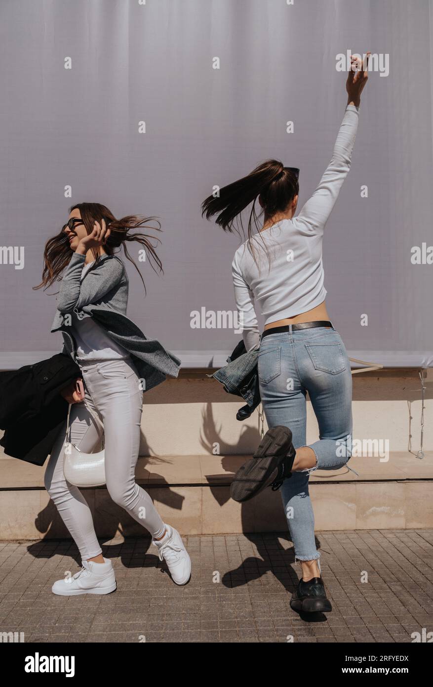 Two beautiful girls dancing and spinning around in front of the grey ...