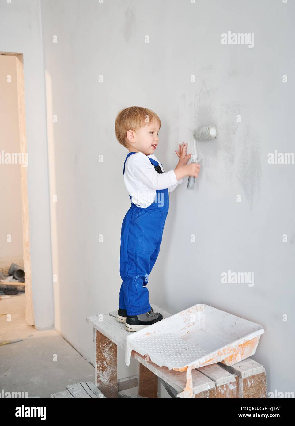 Full length of smiling little boy construction worker painting wall in ...