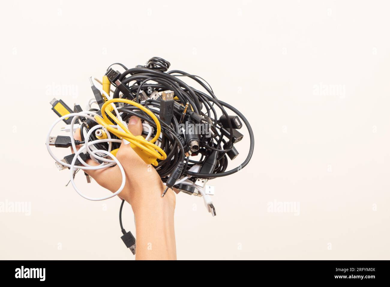 Hand held up with pile of tangled old smart technology wires, used charging cables and cords. E ...