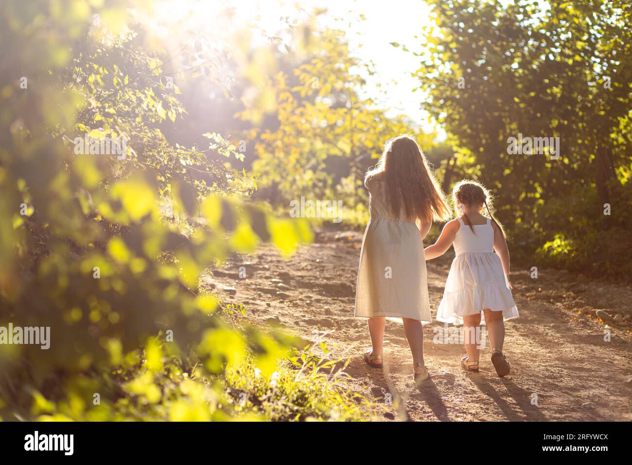 Two little girls, sisters walking outdoors in white dresses, holding ...