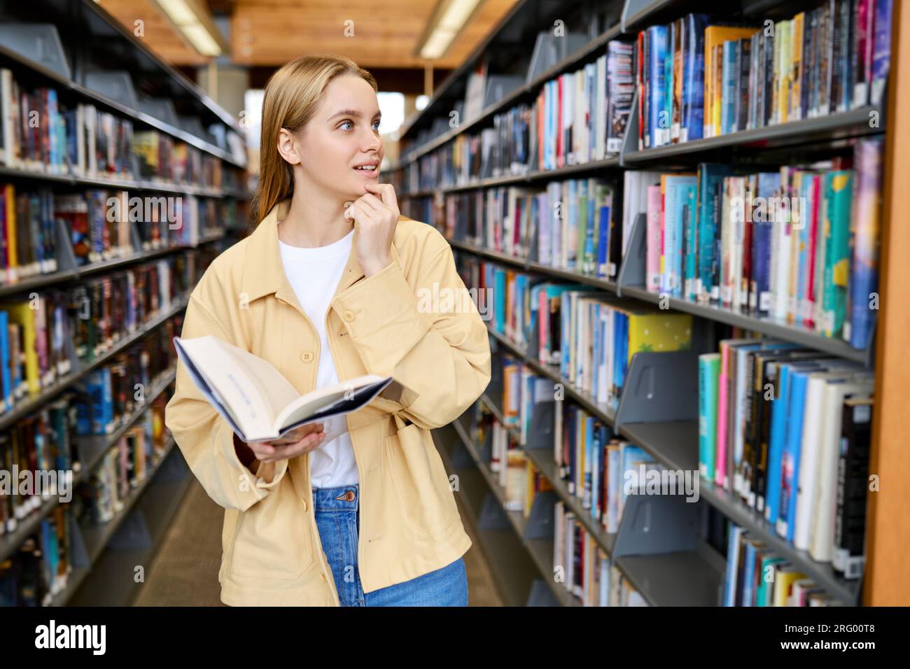 Smart girl student holding book standing in university library or ...