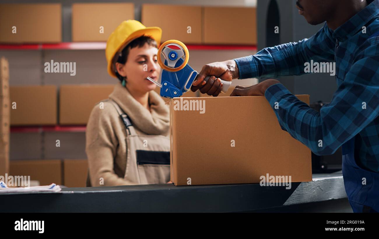 Young depot worker putting adhesive tape on packages, preparing order ...
