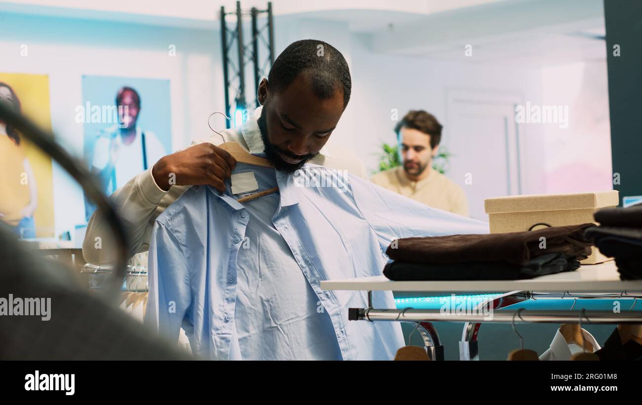 Male retail customer picking up clothes from racks, looking at ...