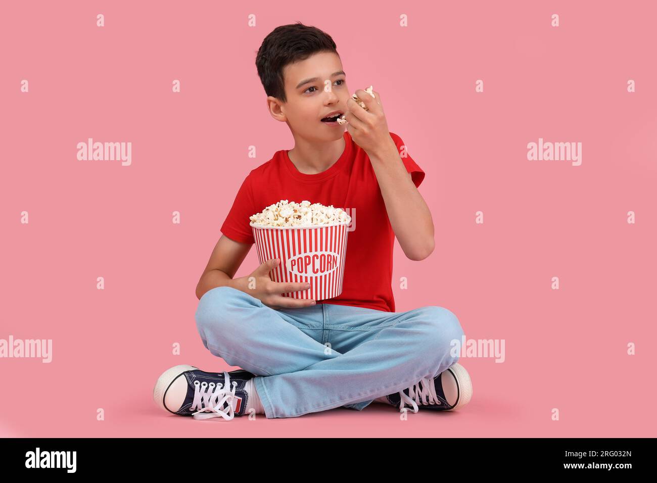 Cute little boy eating popcorn while sitting on pink background Stock ...