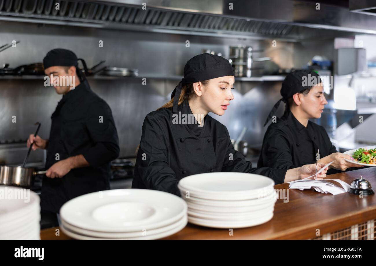 Female chef checks the prepared dish with the paid check in kitchen of ...
