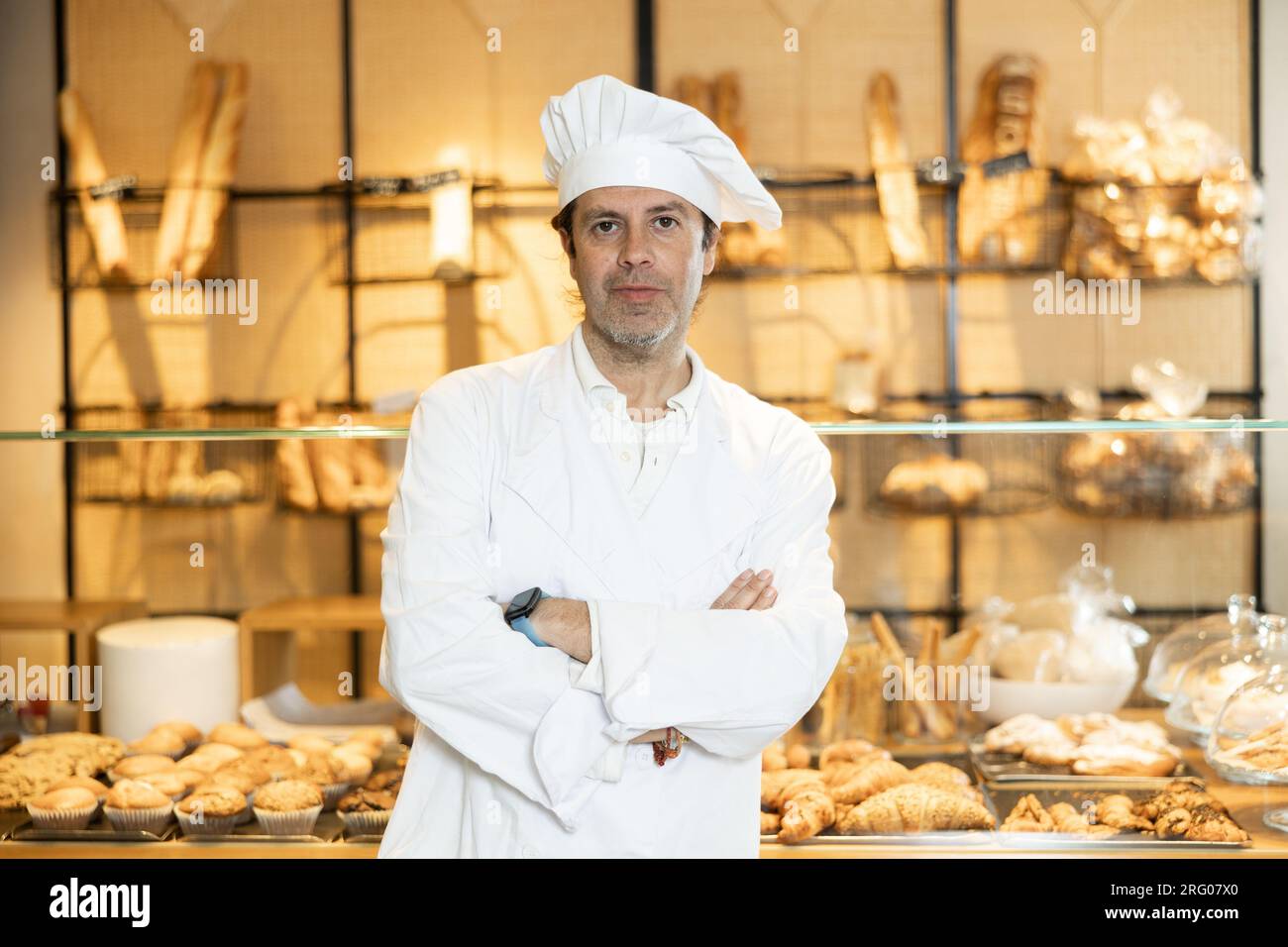Middle-aged male bakery worker in white toque and chef jacket standing ...