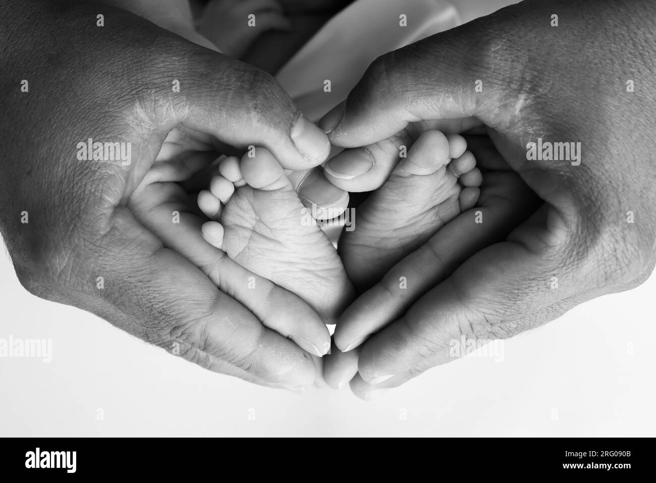 Feet of a tiny newborn on parental heart-shaped hands close-up. Legs ...