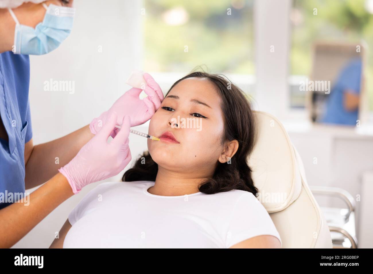 Face of young female client receiving injections during lip enhancement ...