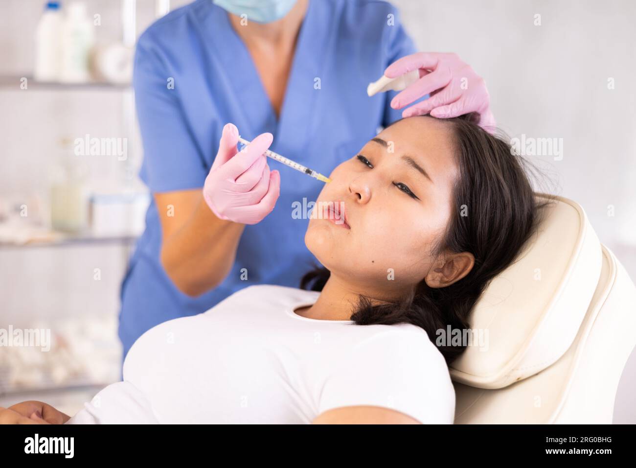 Face of young female client receiving injections during lip enhancement ...