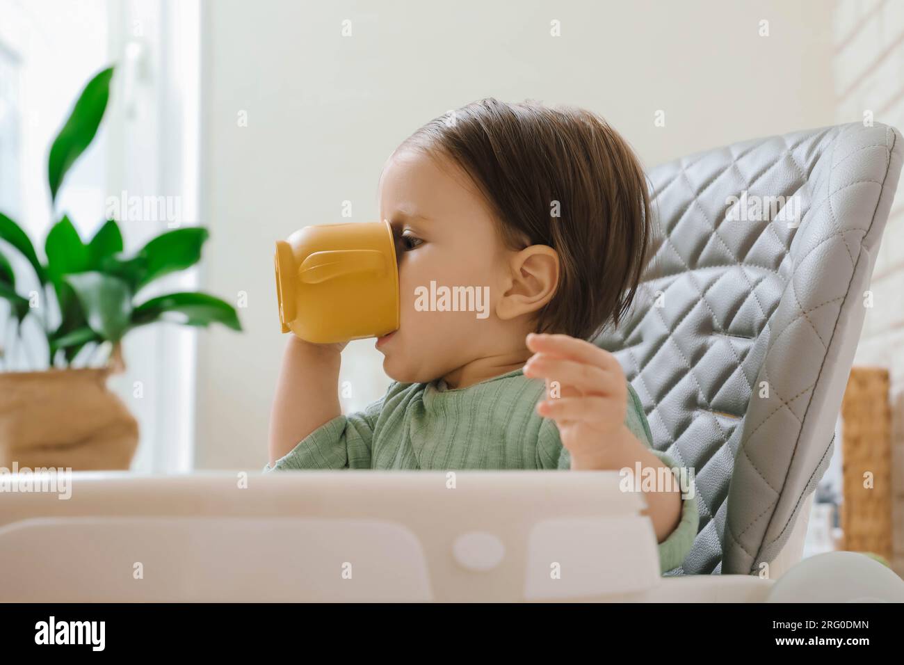 Cute little baby drinking from cup in high chair indoors Stock Photo ...