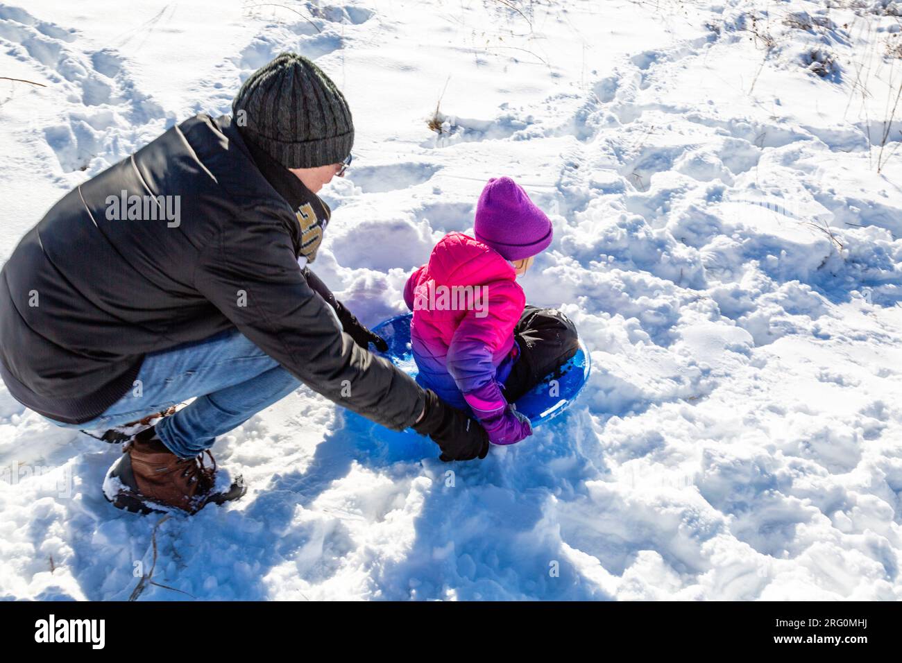 A man pushes his young daughter through the snow on her sled at Metea ...