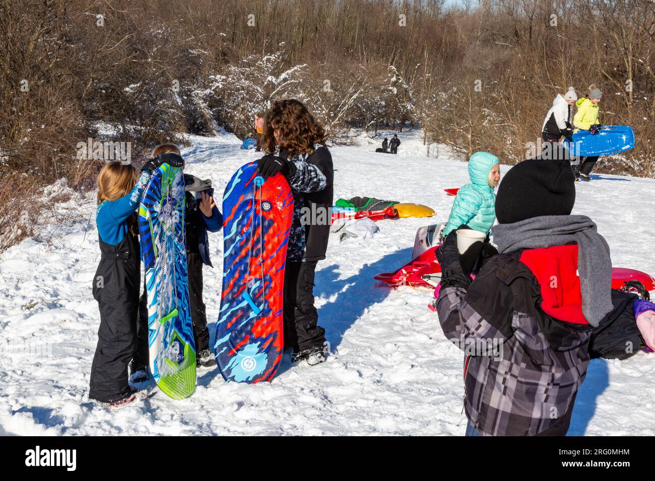A group of young people in heavy coats inspect their colorful sleds ...