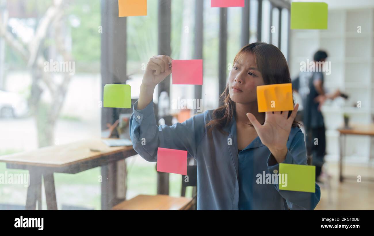 Thoughtful woman hand writing paper note, sticky note on glass window ...