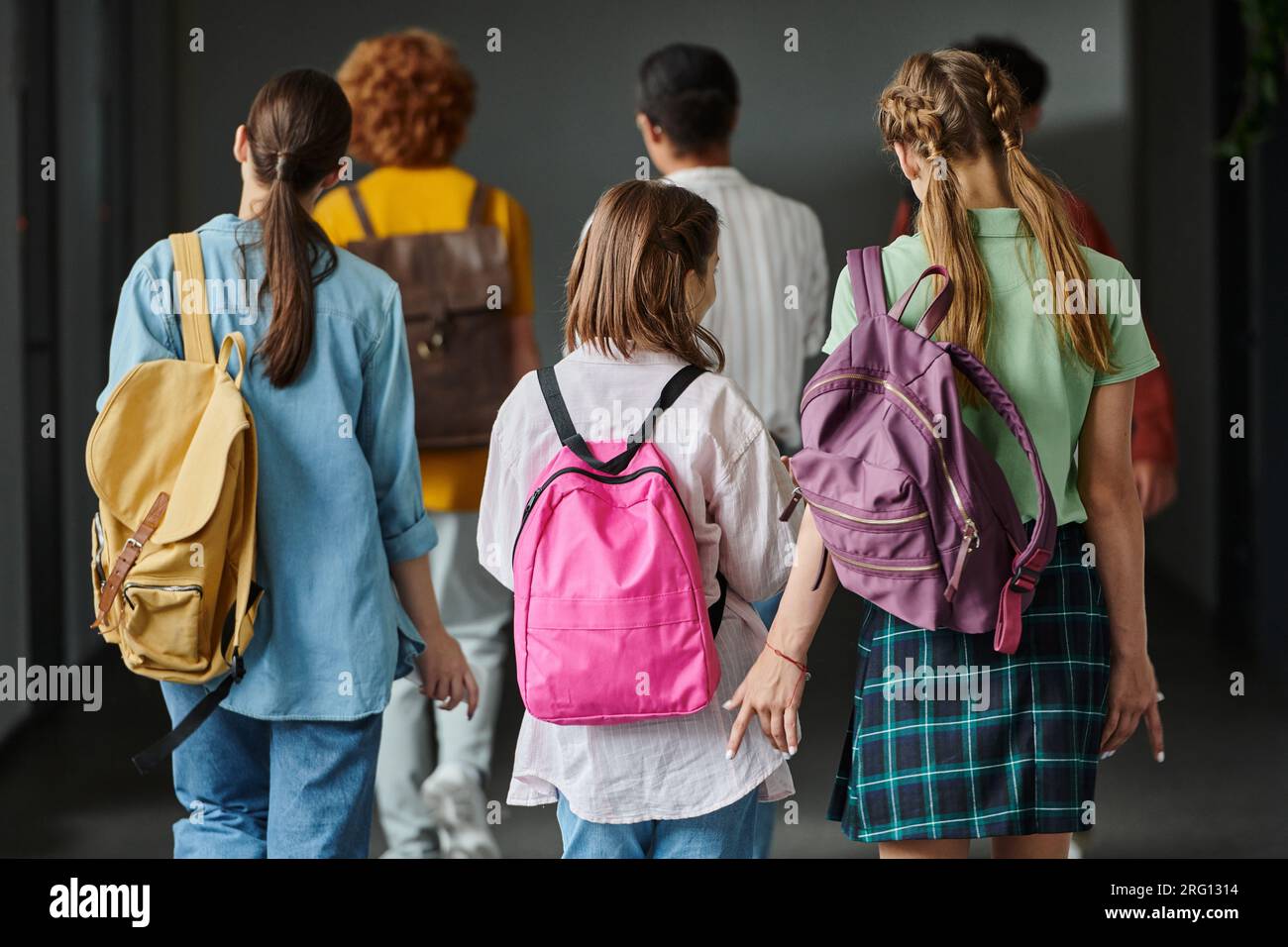 back view of schoolkids walking in hallway of school between classes ...