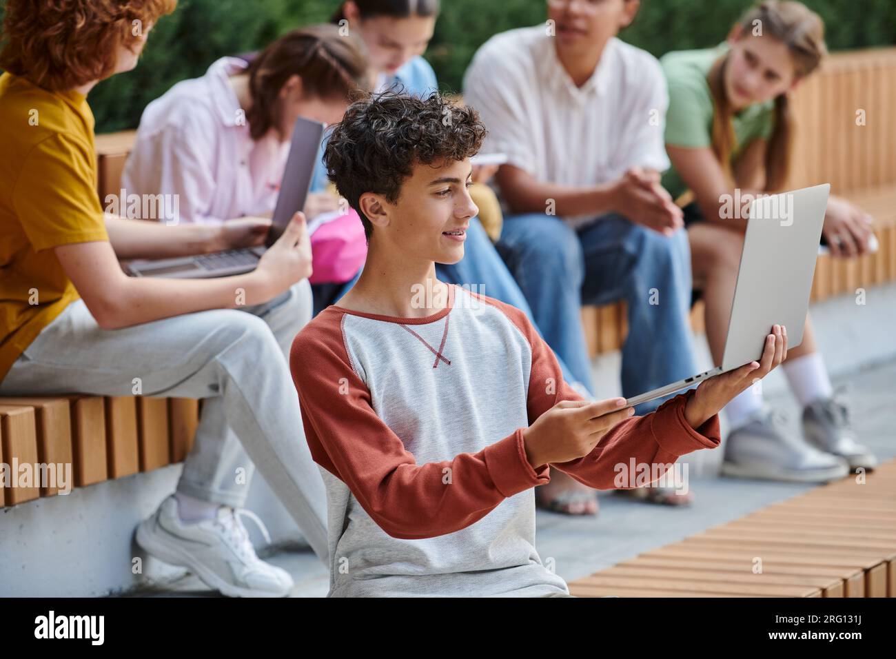 teenage boy using laptop near classmates and teacher, blur, diversity ...