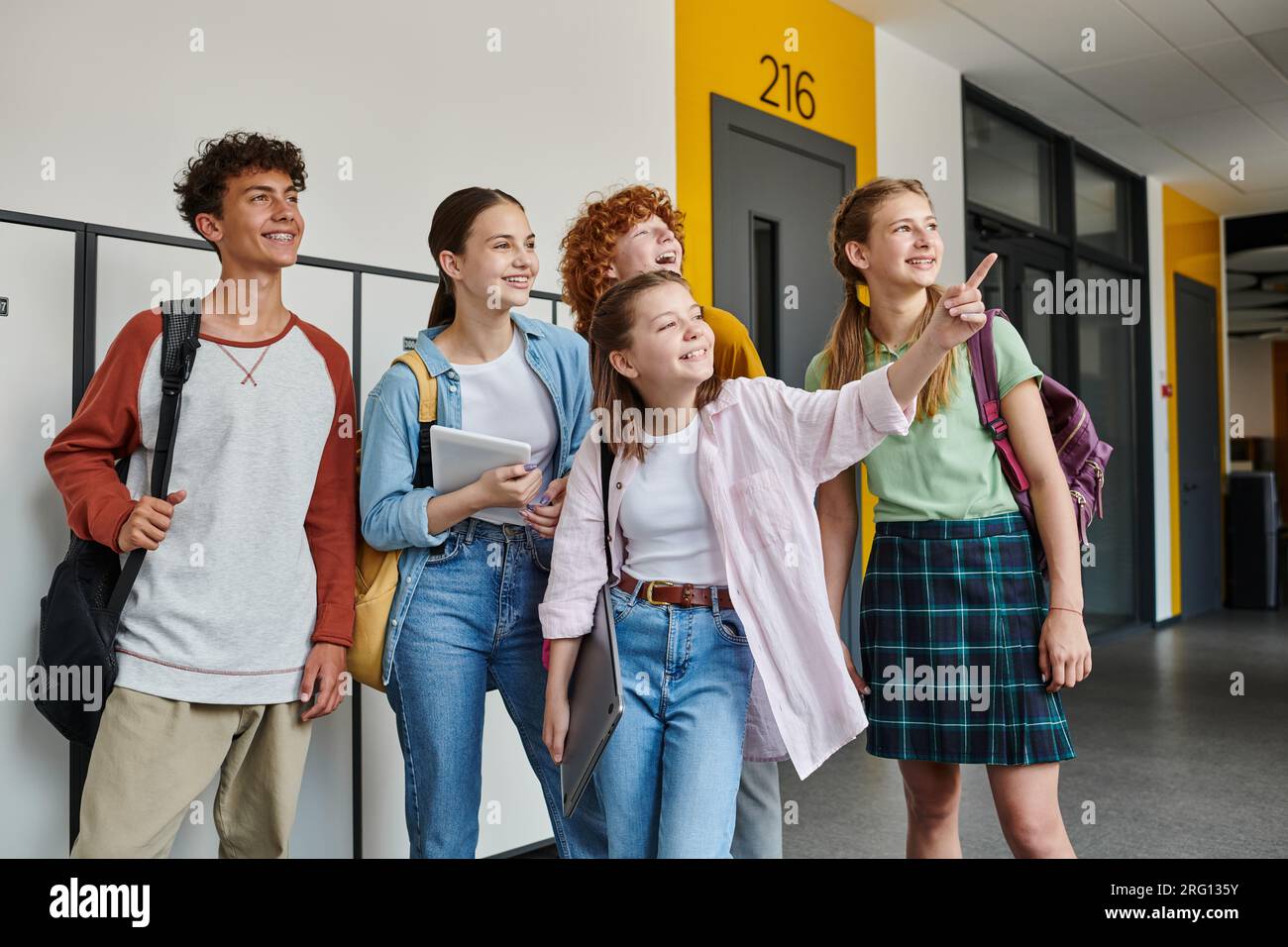 happy teen students looking away in school hallway, schoolgirl pointing ...