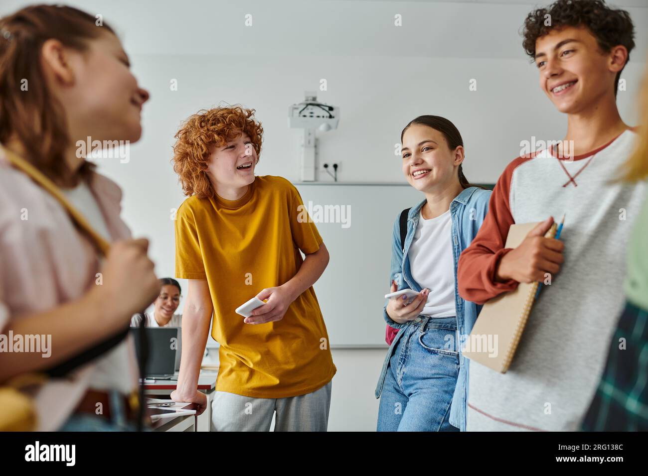 Positive classmates with devices and notebook talking while standing in ...