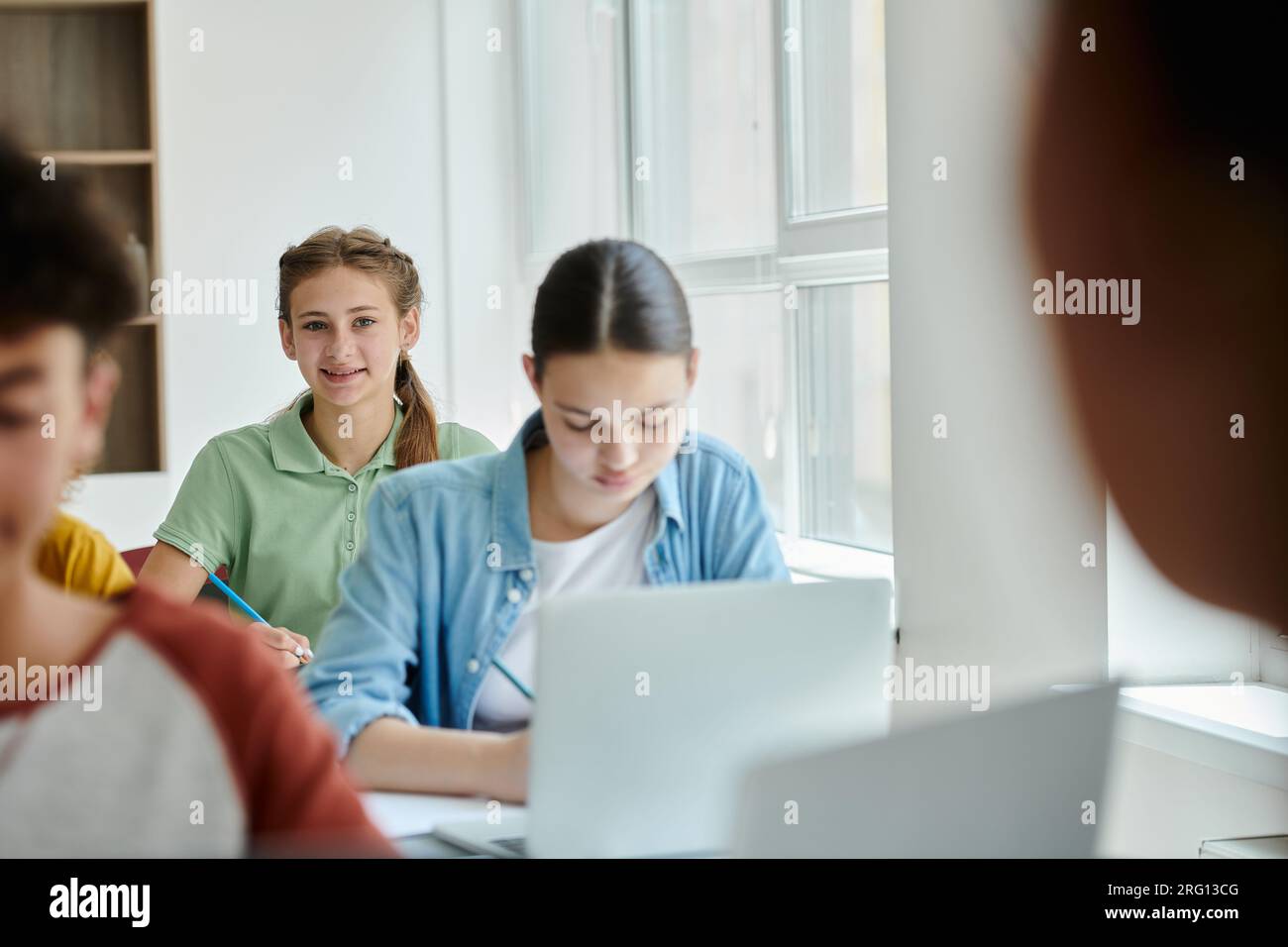 Teen schoolgirl looking at camera and smiling near blurred classmates ...