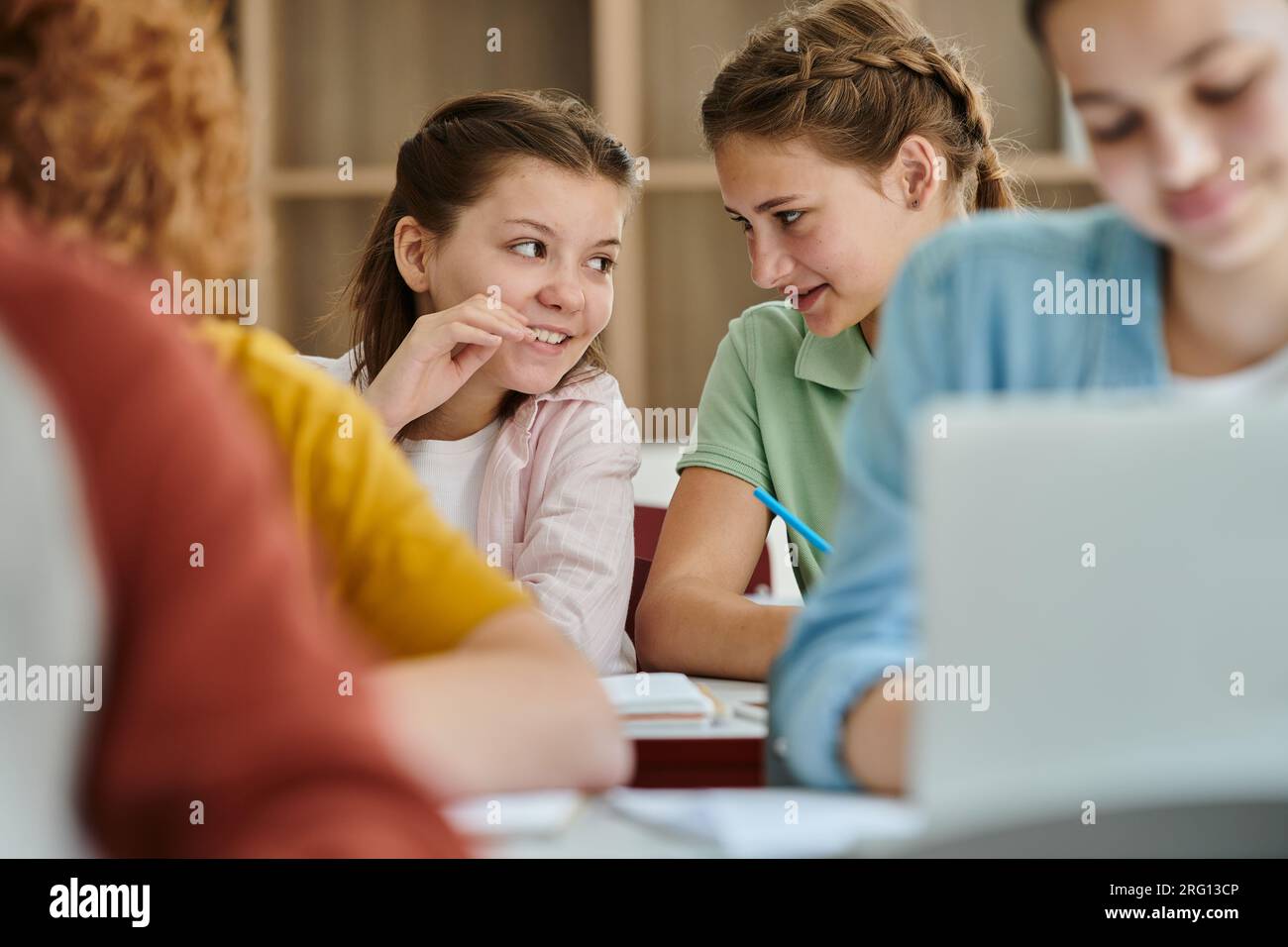 Smiling teenage schoolgirls talking near classmates during lesson in ...