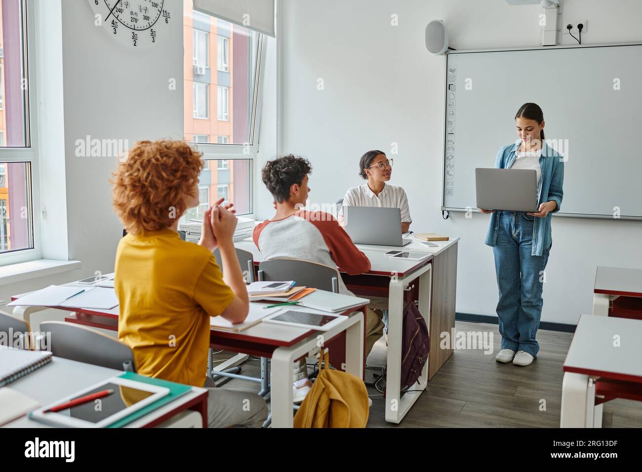 Teen schoolgirl holding laptop during lesson near african american ...