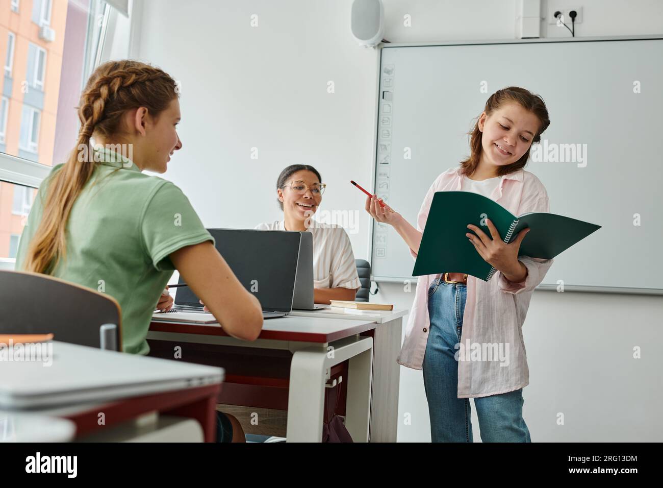 Smiling schoolgirl talking and holding notebook near african american ...
