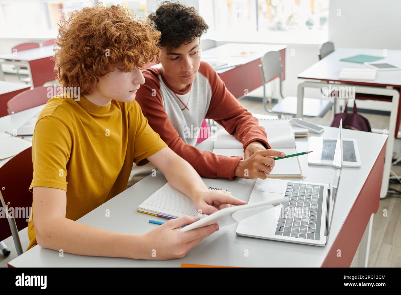 Teenage schoolboys using devices together during lesson in classroom at ...