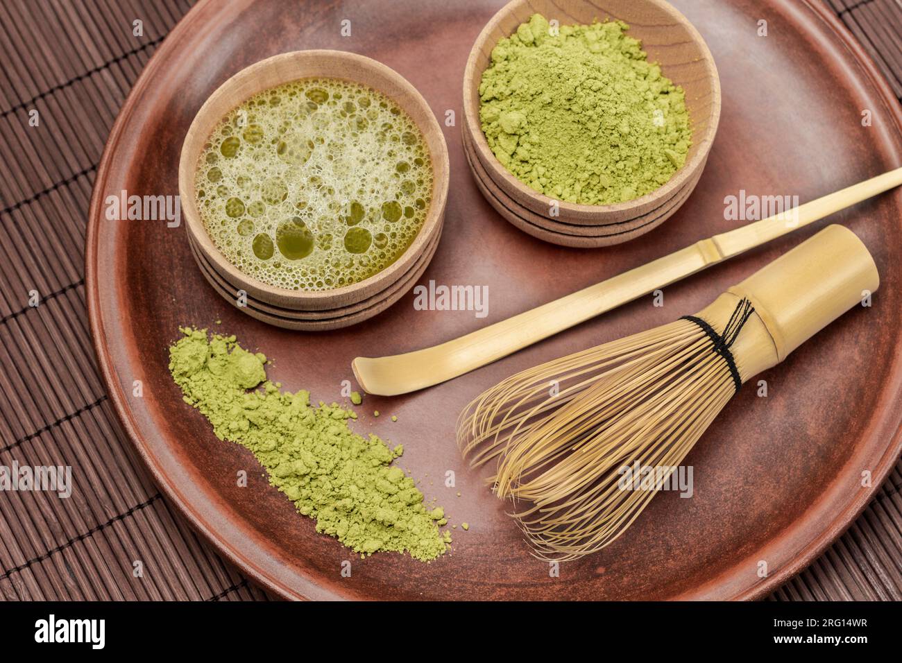 Matcha tea powder and tea in wooden bowls. Bamboo whisk and spoon on a ...