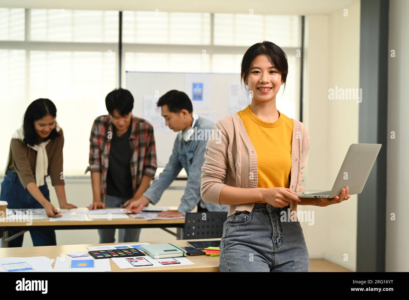 Portrait of smiling asian female web developer holding laptop standing ...