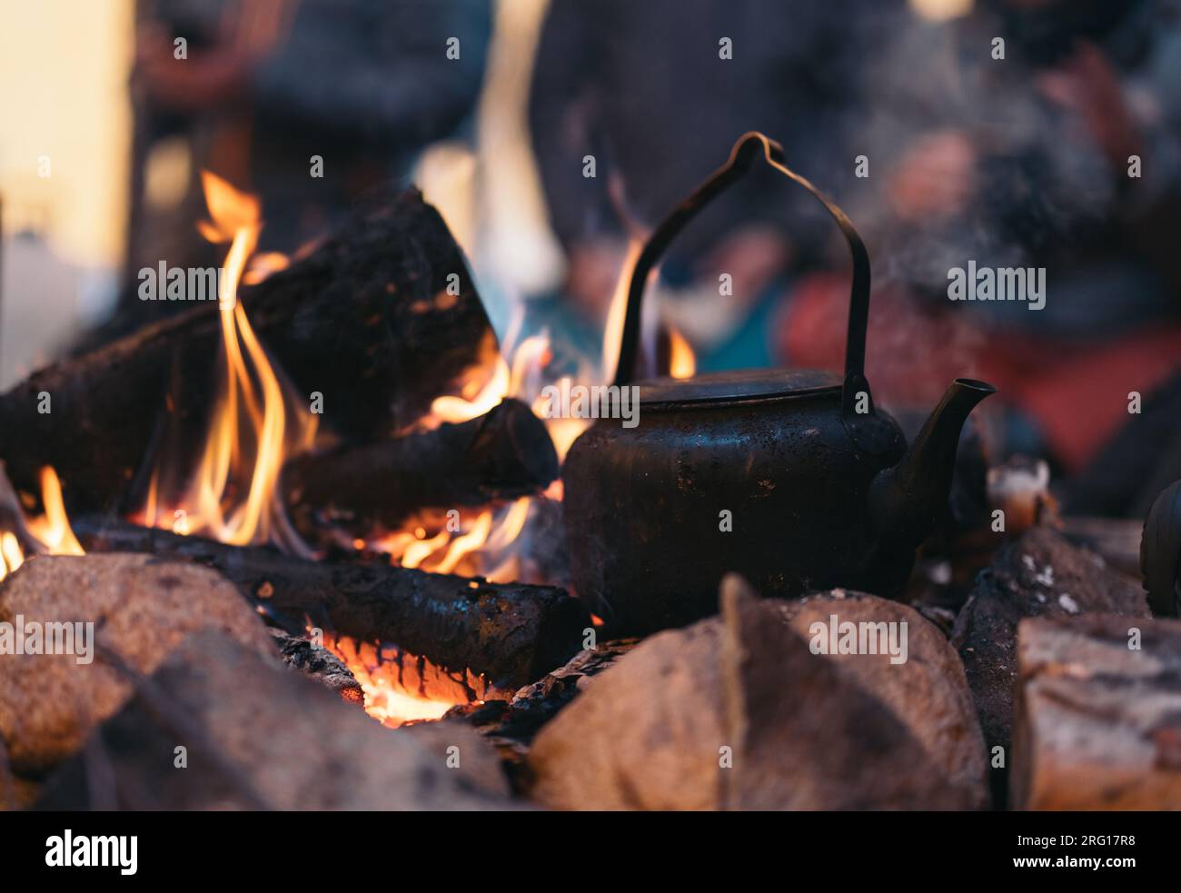 Black metal kettle on burning bonfire with hot flames at campsite ...