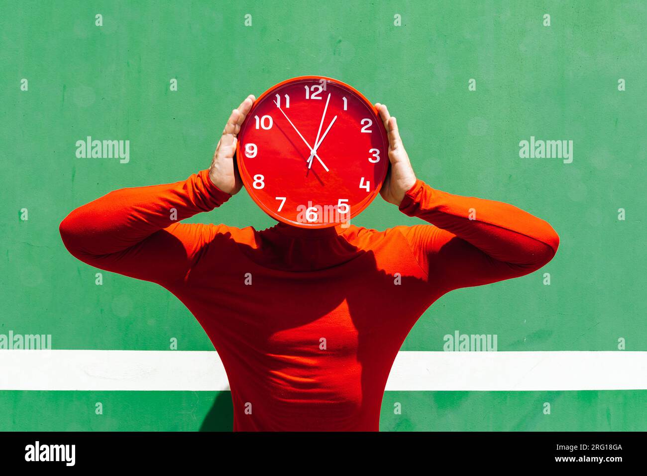 Unrecognizable person in red outfit holding big round clock hiding face ...