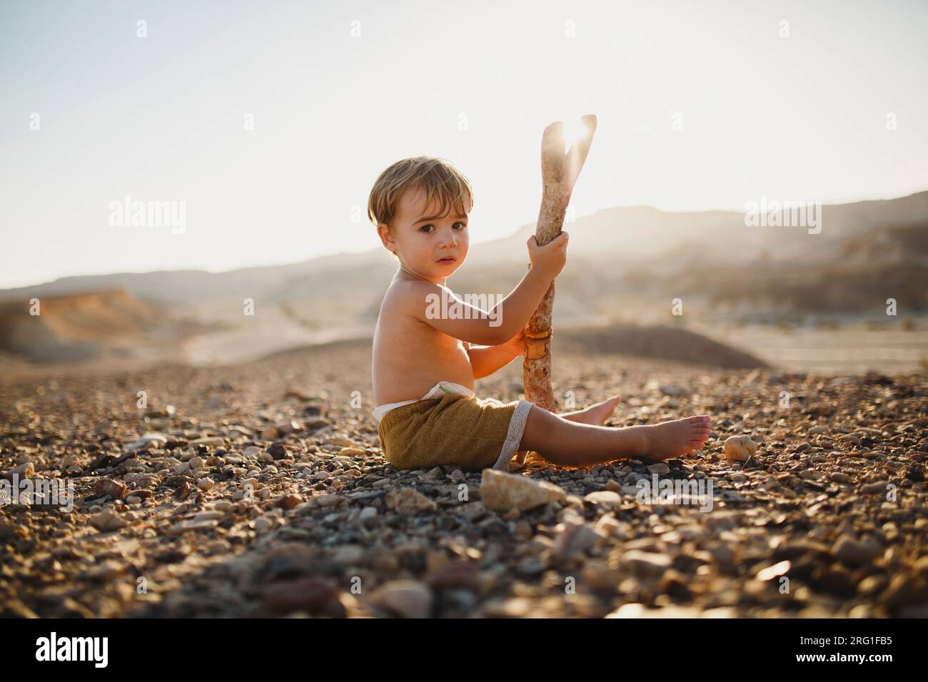 Toddler boy sitting on the desert's ground holding a branch Stock Photo ...