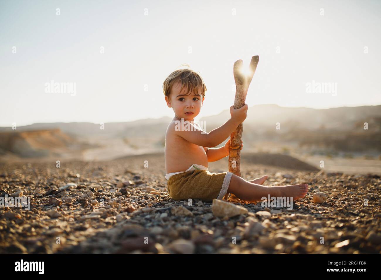 Toddler boy sitting on the desert's ground holding a branch Stock Photo ...