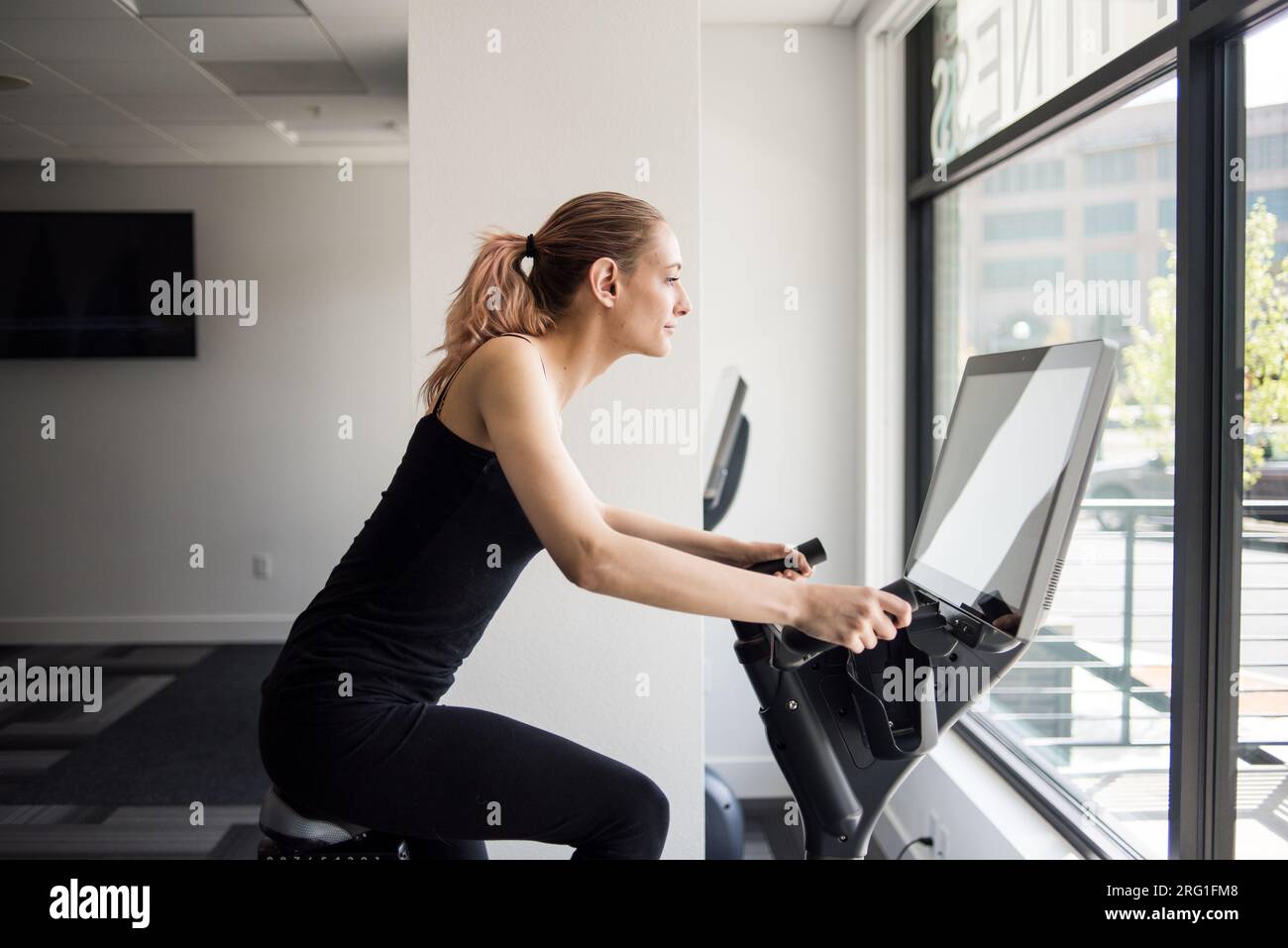 Woman riding exercise bike in workout room looking out window Stock ...