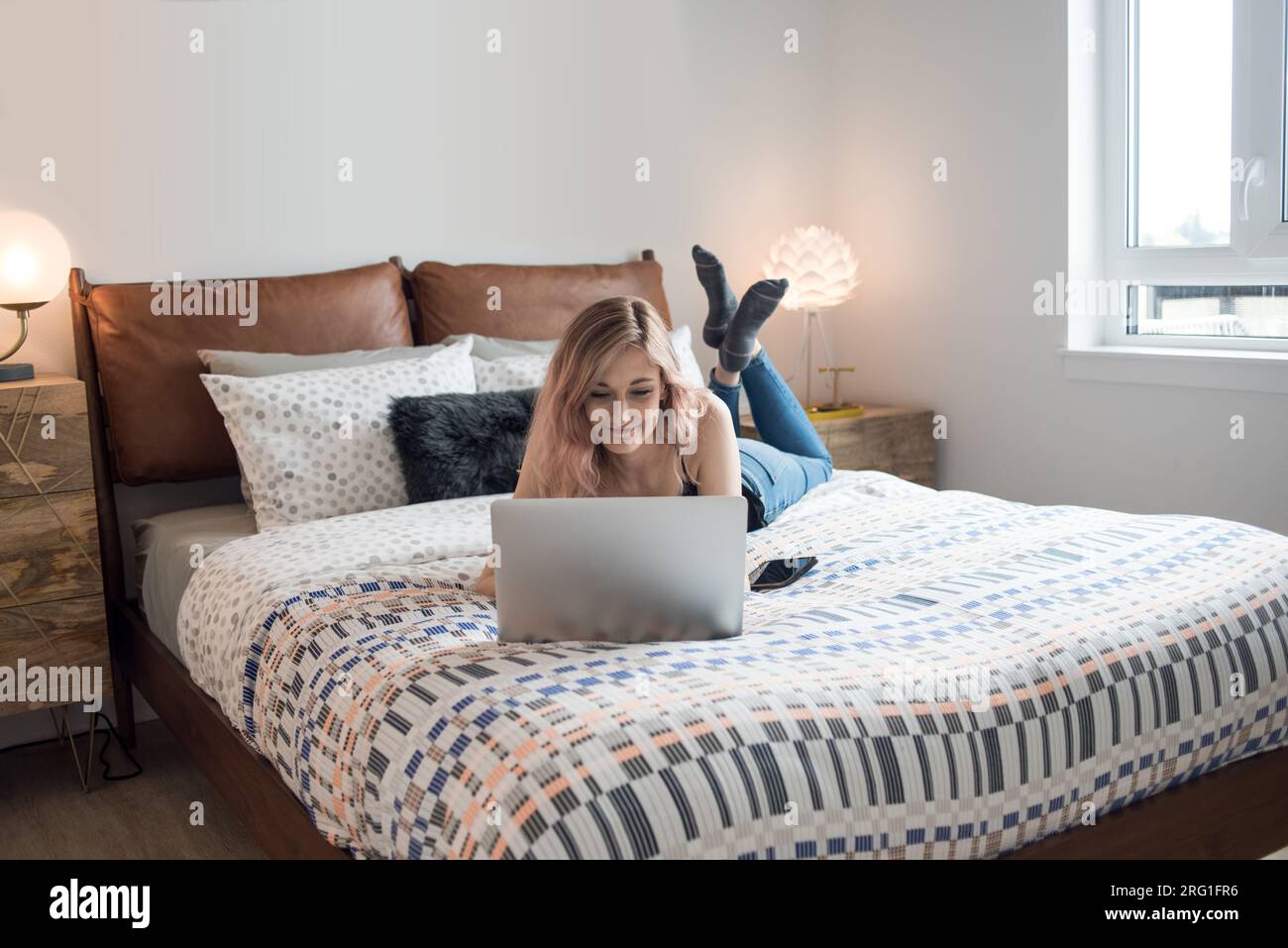 Millenial woman lying on bed using computer Stock Photo - Alamy