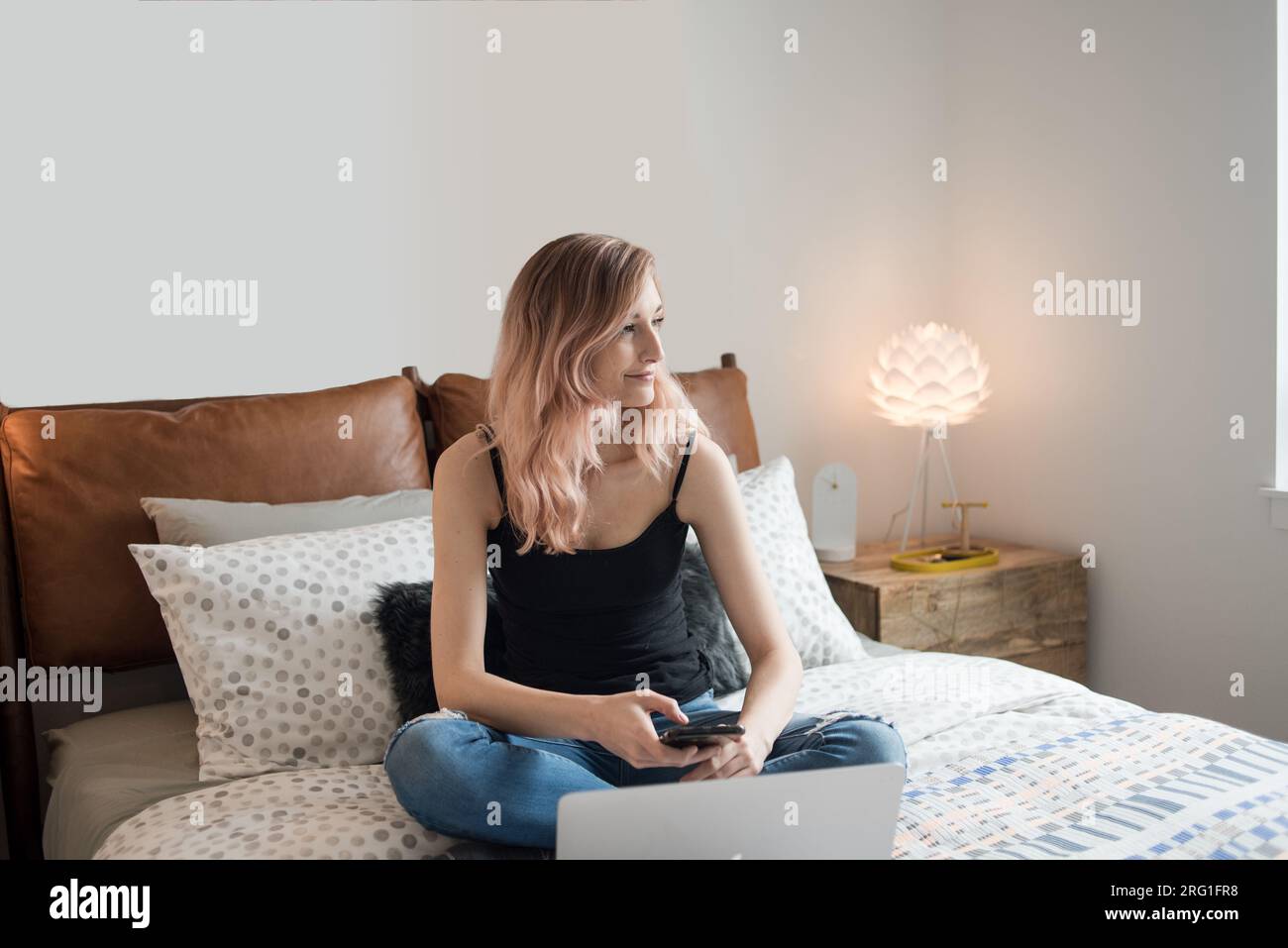 Woman looking off camera while sitting on bed Stock Photo - Alamy