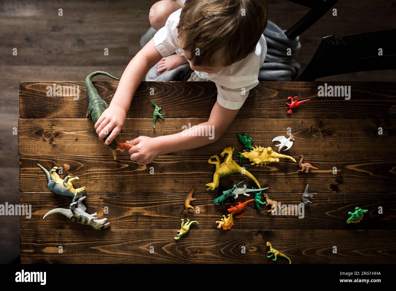 Boy playing with toy dinosaurs at table Stock Photo - Alamy