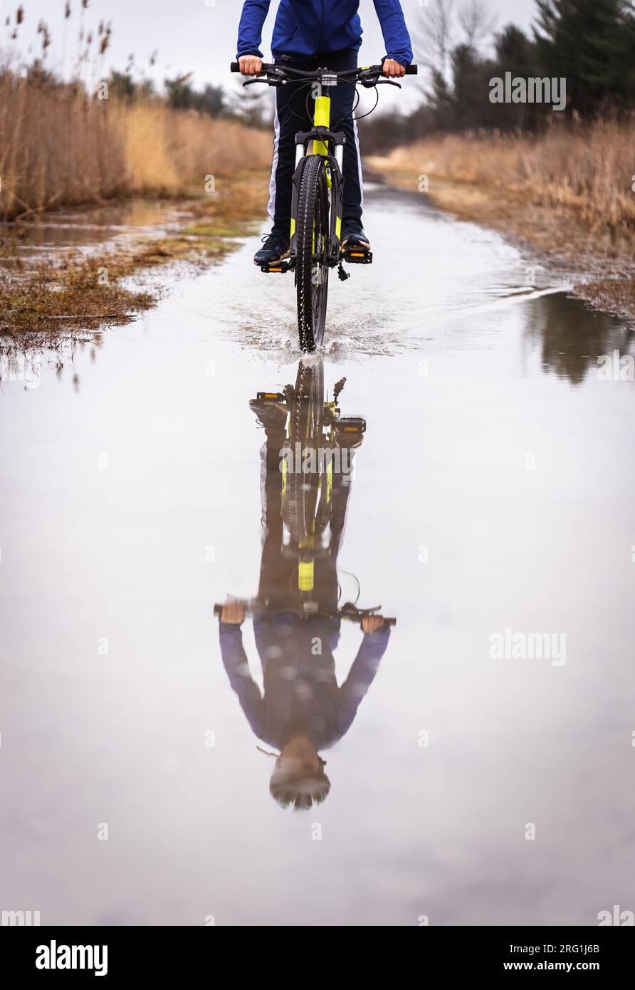 Crop of boy riding bike in puddle on flooded trail with reflection ...