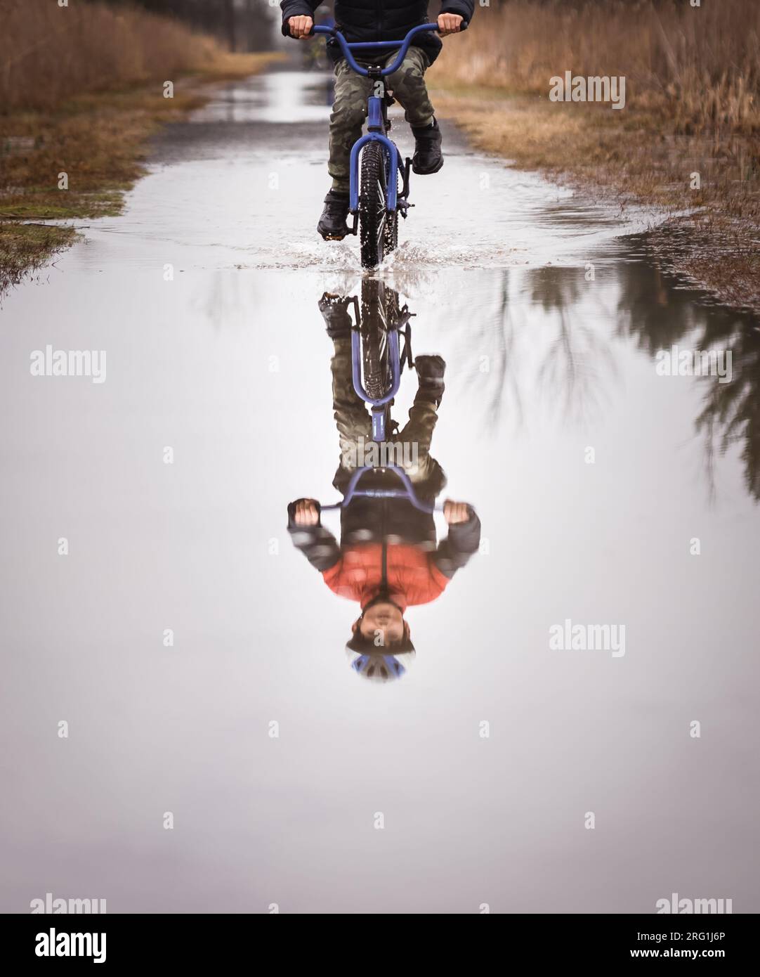 Crop of boy riding bike in puddle on flooded trail with reflection ...