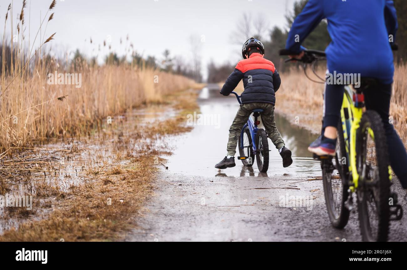 Two boys riding their bikes through a large puddle on a flooded trail ...