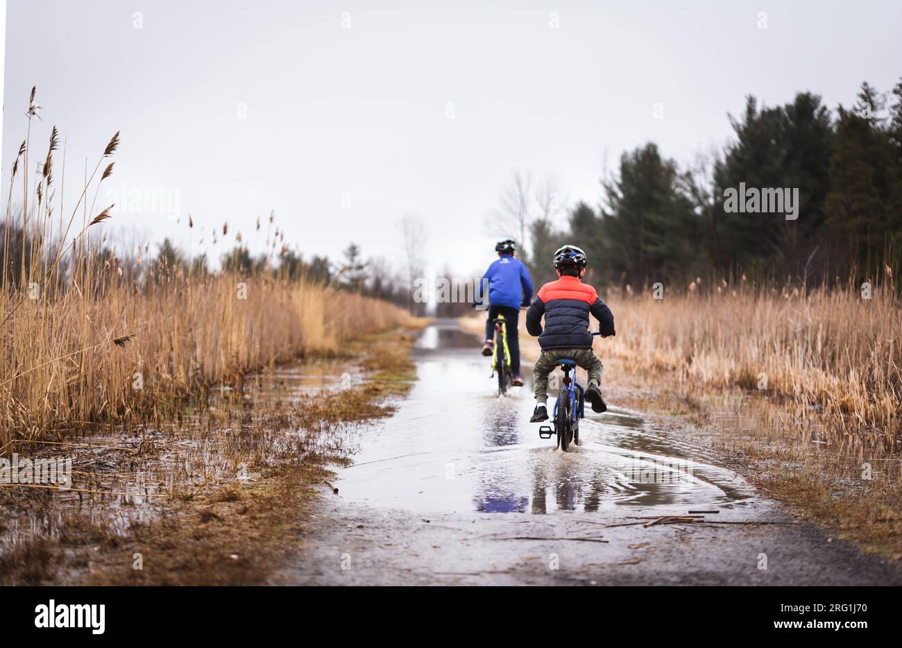 Two boys riding their bikes through a large puddle on a flooded trail ...