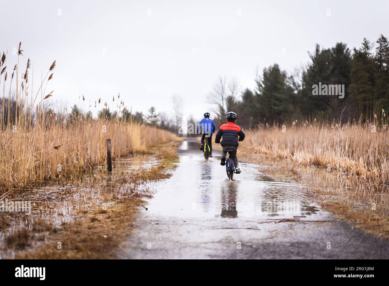 Two boys riding their bikes through a large puddle on a flooded trail ...