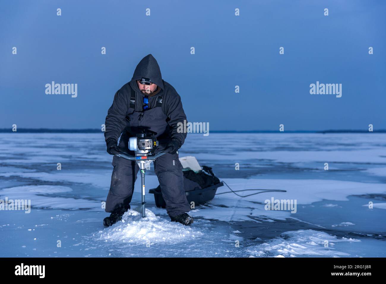 Fisherman drilling hole in the ice Stock Photo - Alamy