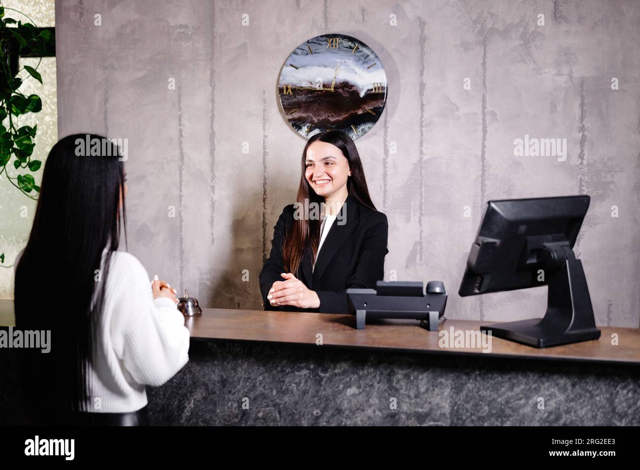 Friendly young concierge standing behind a reception counter talking ...