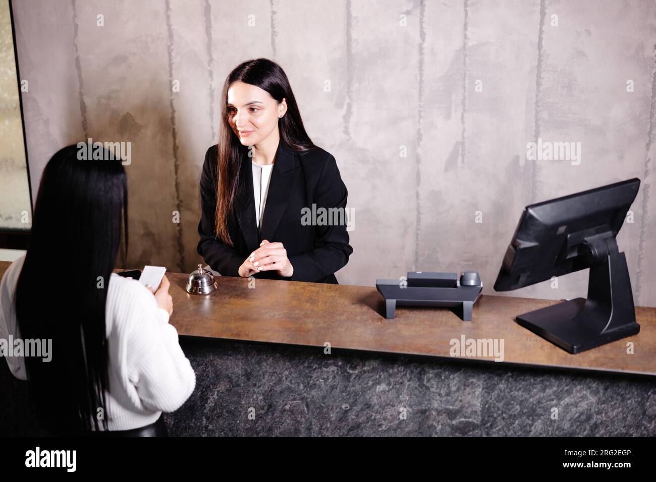 Friendly young concierge standing behind a reception counter giving ...